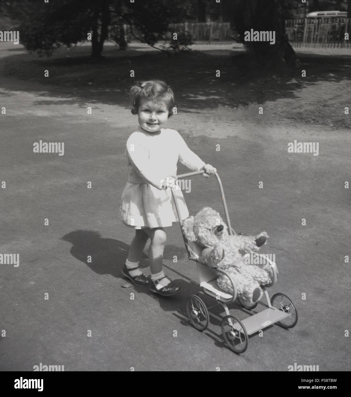 1950s, historical, young girl outdoors in a park pushing her toy metal ...