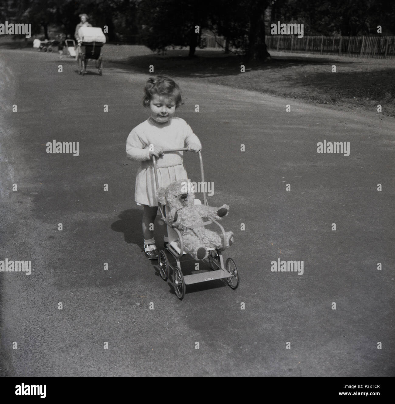 1950s, historical, young girl outdoors in a park pushing her toy metal ...