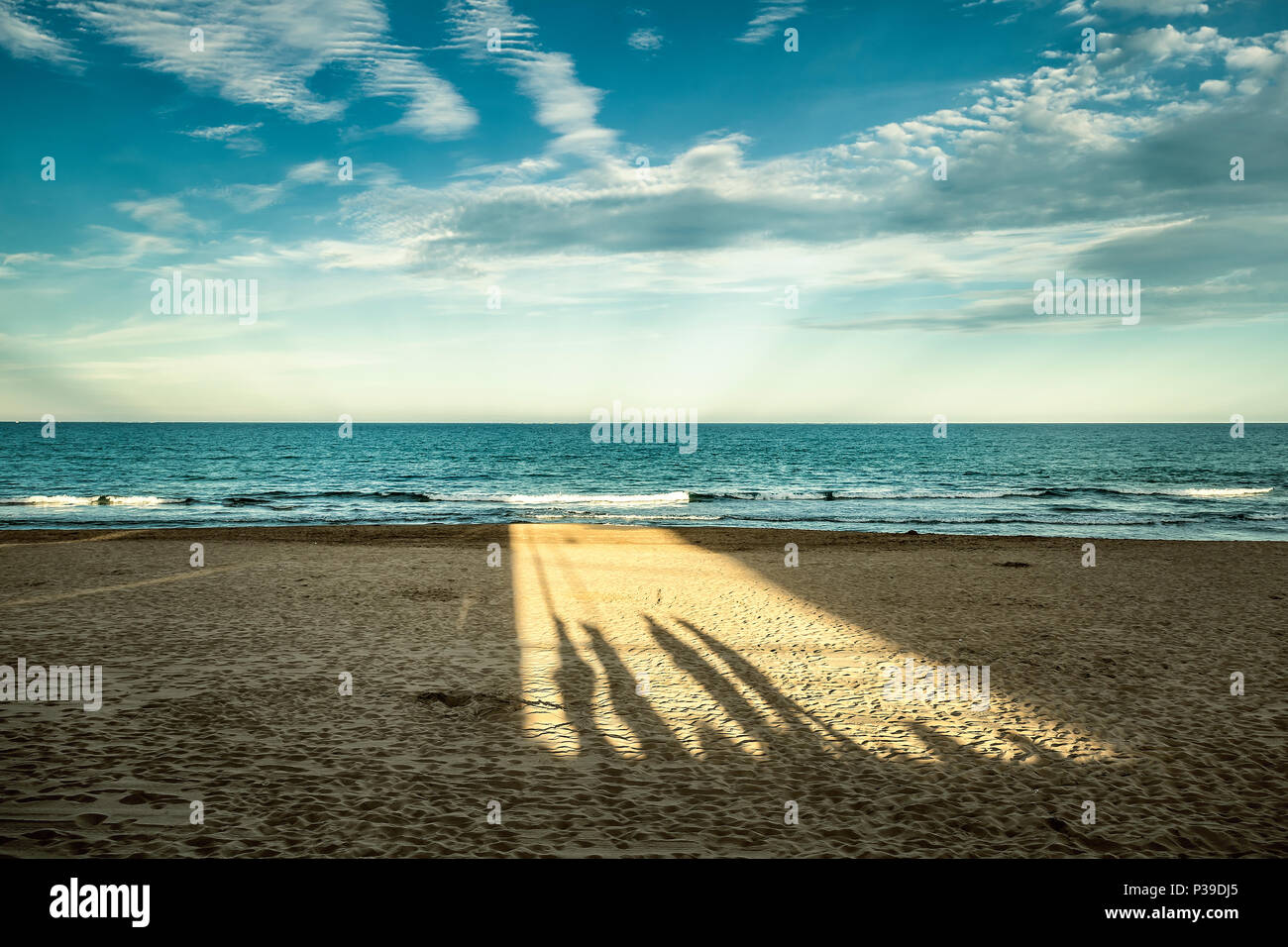 last rays of sunshine on the beach with shadows of peoples in the sand ...
