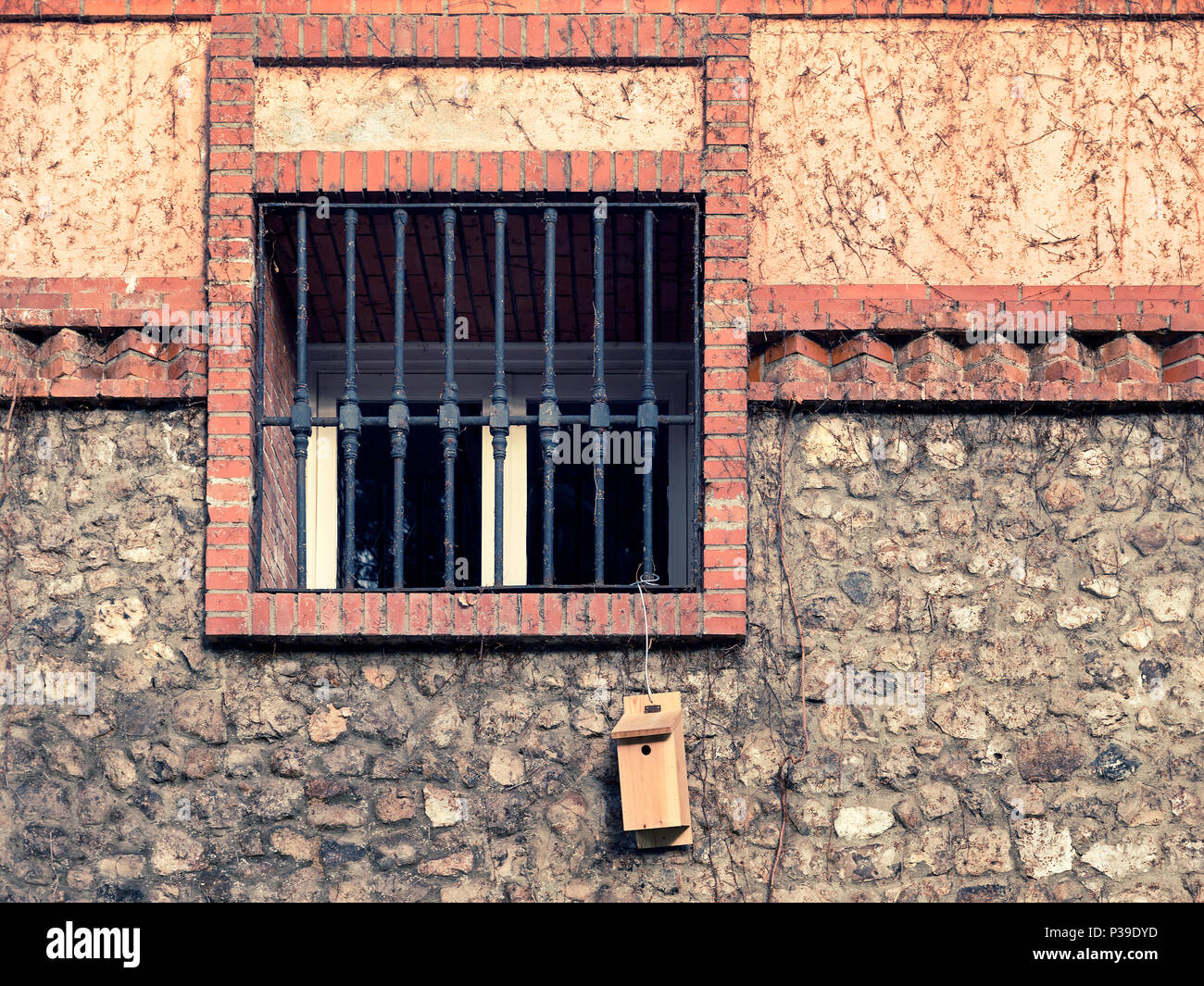 window with iron grating on a rustic facade and a small wooden house ...