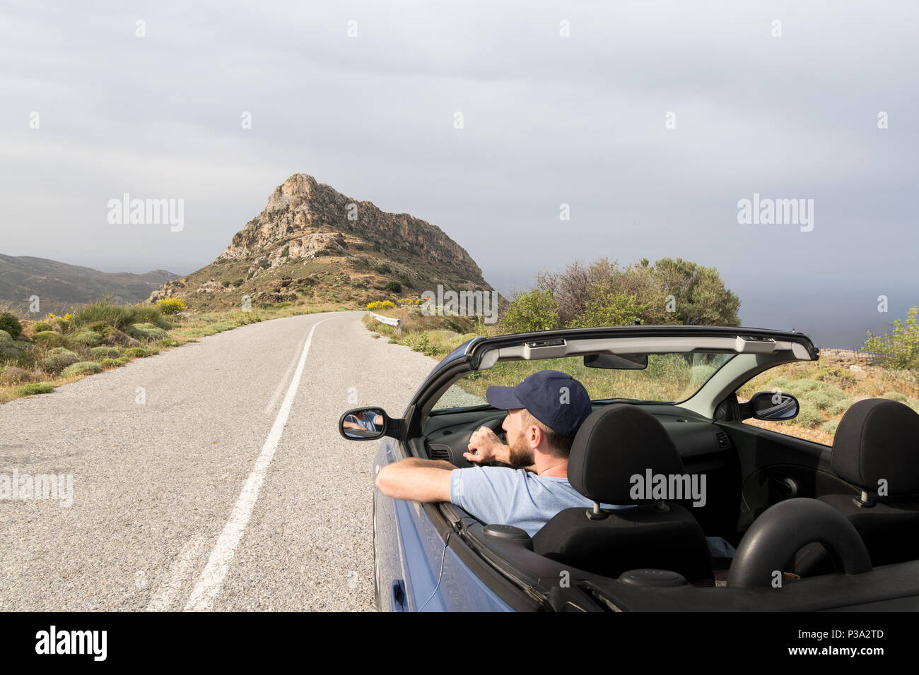 Young man driving in convertible blue car without roof on mountain road ...