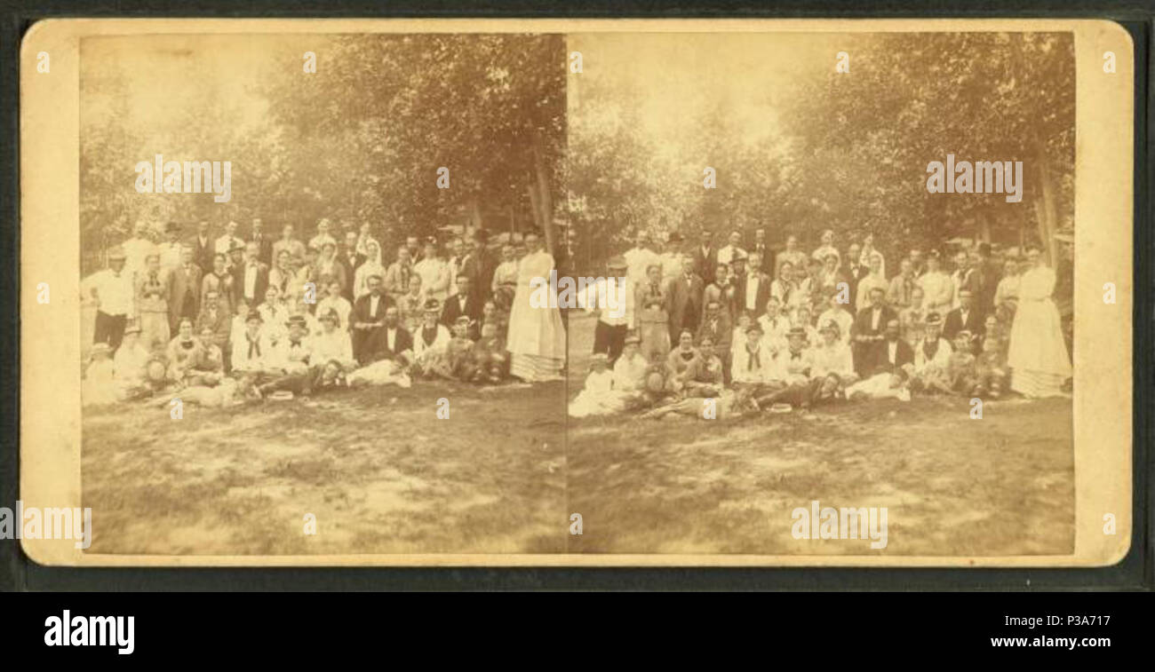 . Large group of men, women and children on a lawn under some trees ...