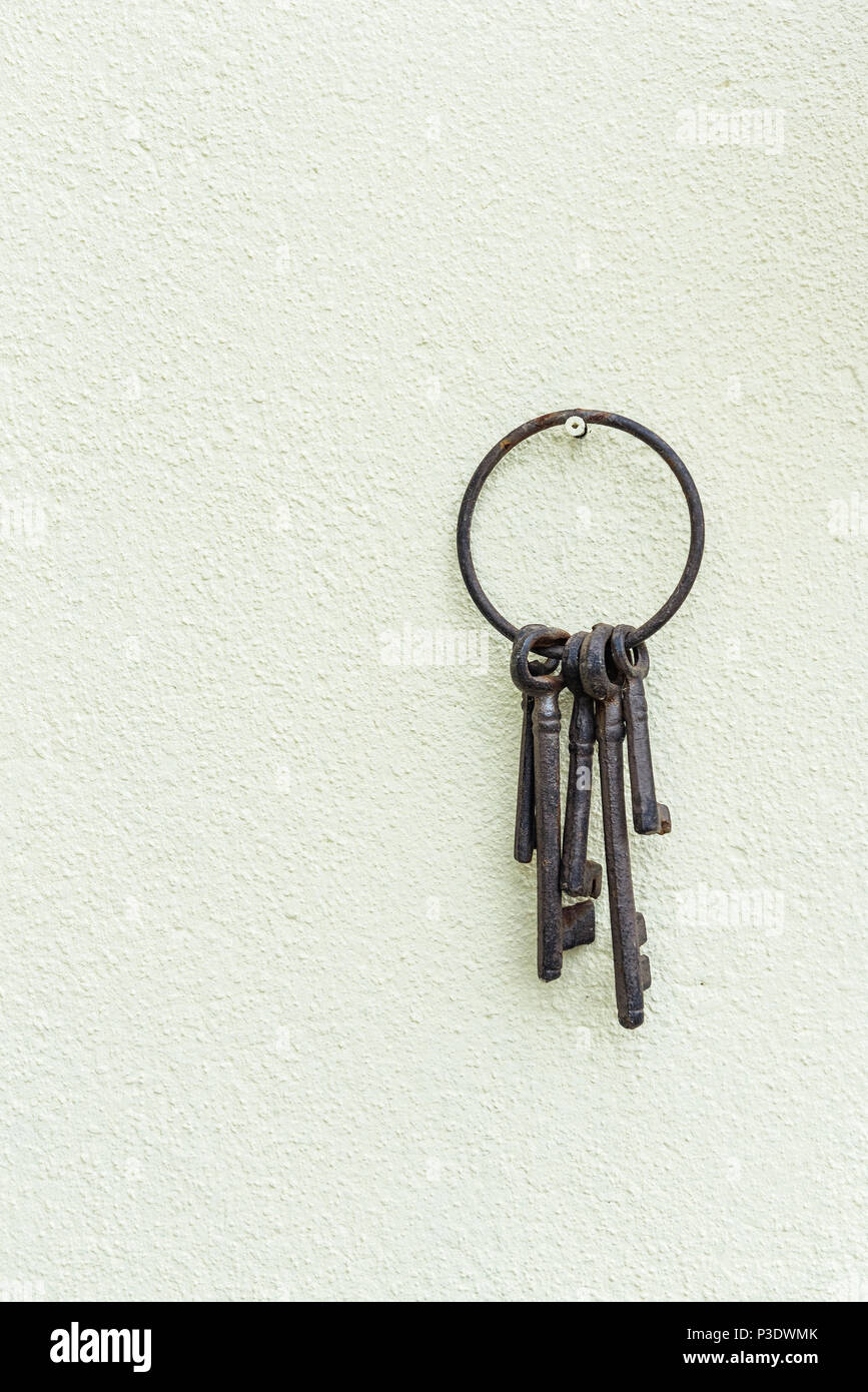 Rusty old keys hanging on a cream textured wall. Corroded metal keyring ...