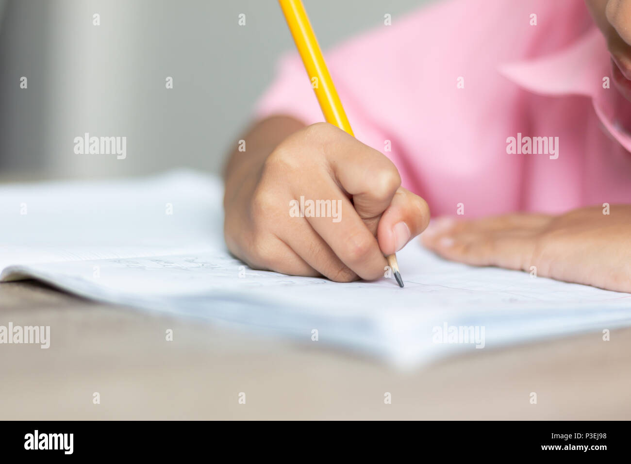 Close up a little girl doing homework. Hand is holding a yellow pencil ...