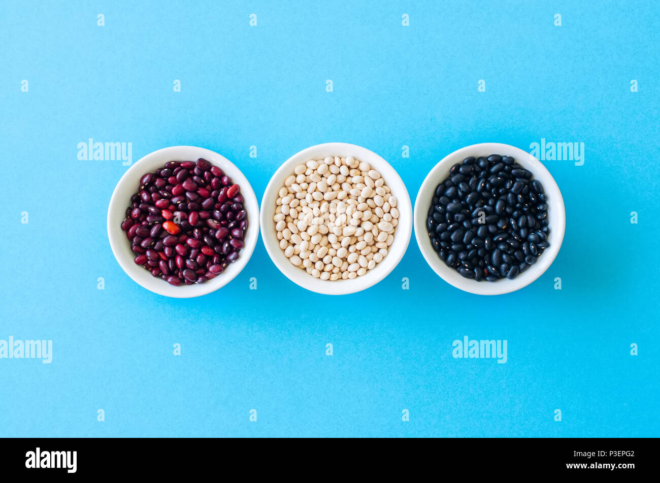 Tree types of raw beans in a white bowls on a light blue background ...