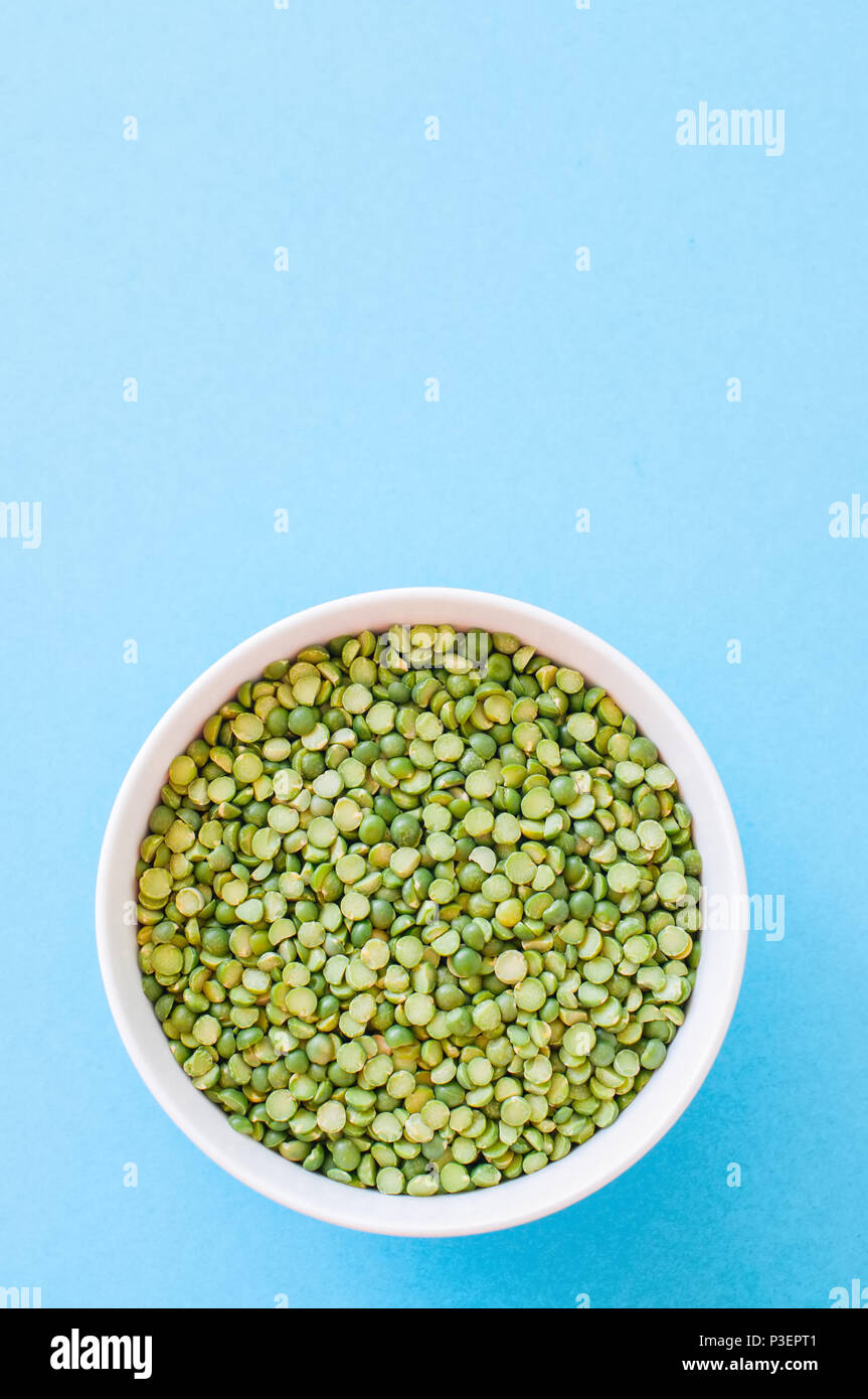 Raw uncooked green peas in a white bowl on a light blue background. Top ...