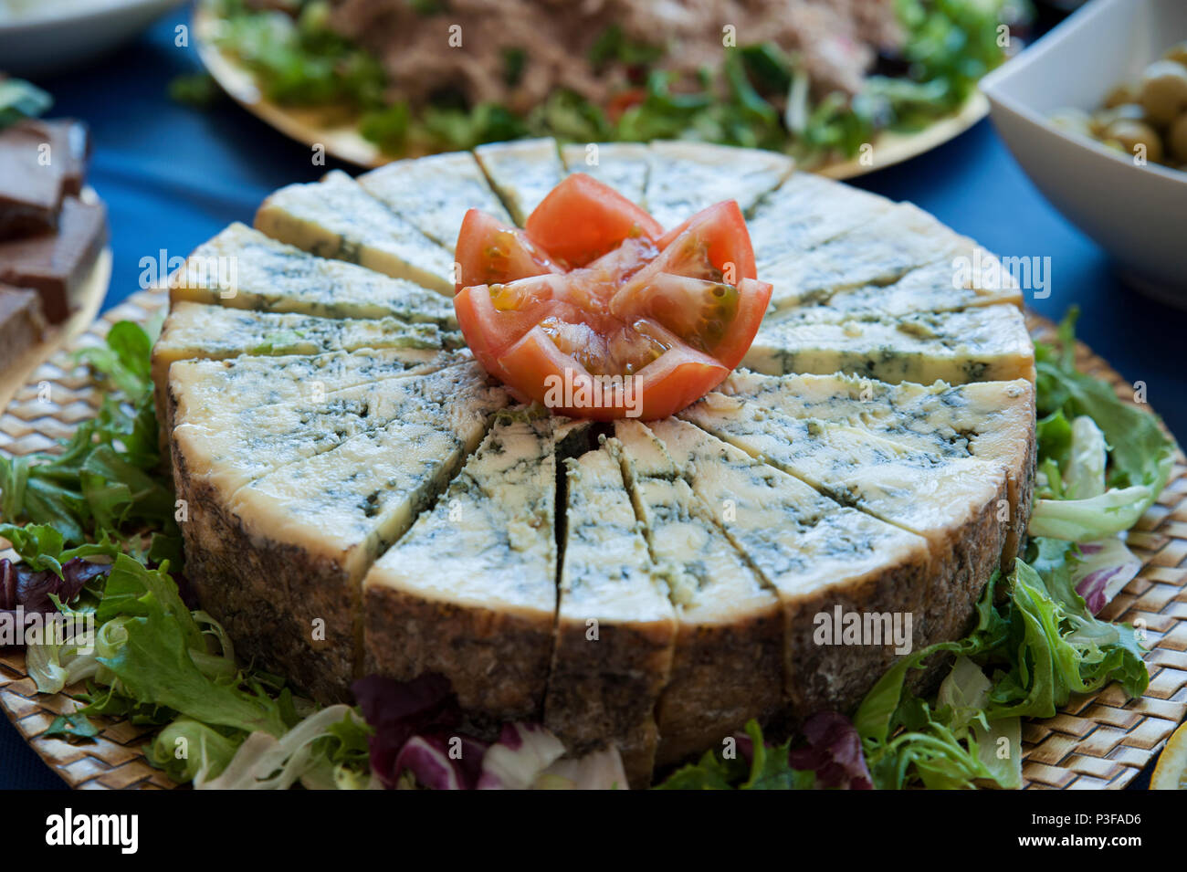 Horizontal shot of aged blue cheese wheel, cut in small triangles at a ...