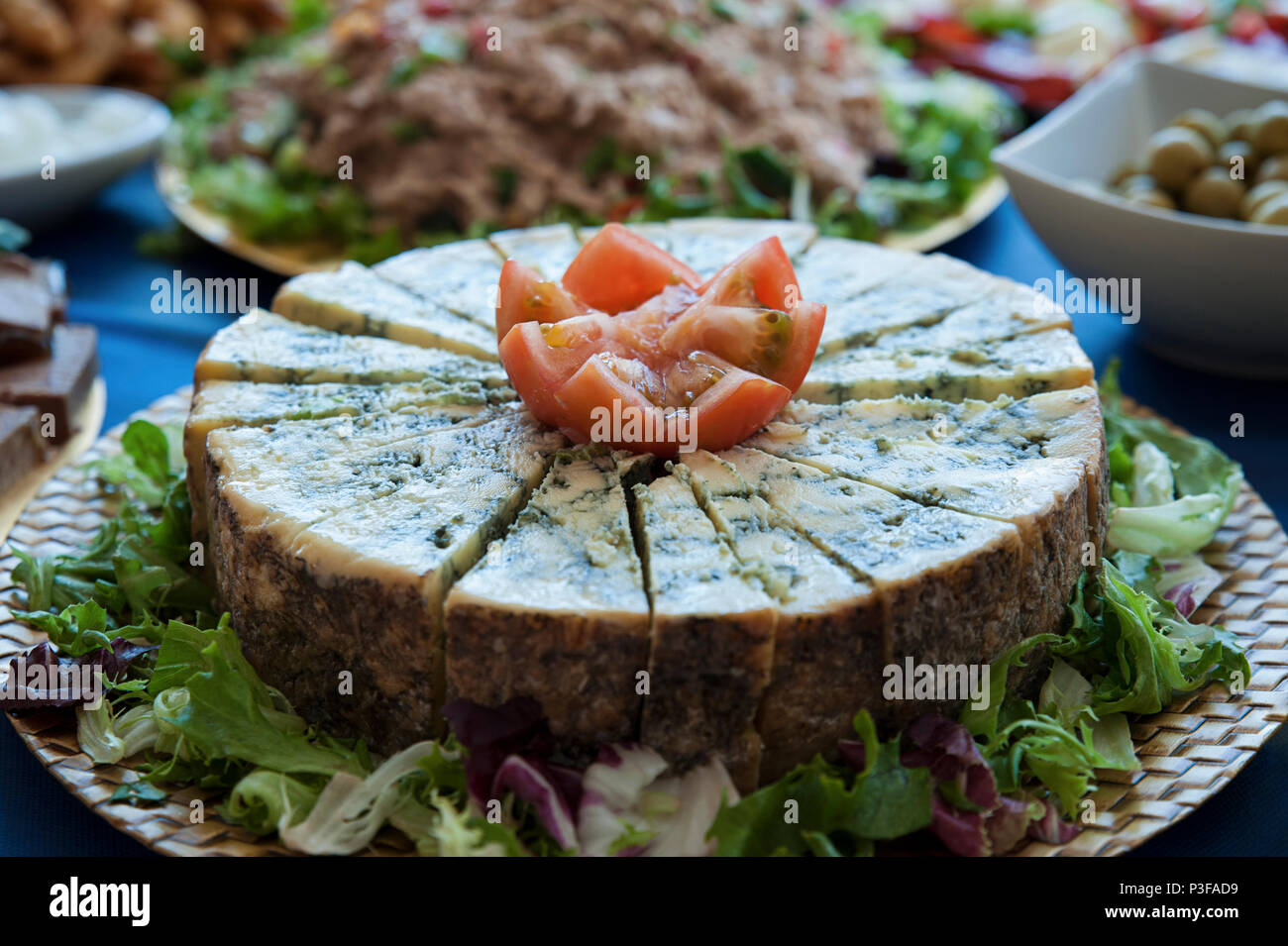 Aged blue cheese wheel with wedge, cut in small triangles at a buffet ...