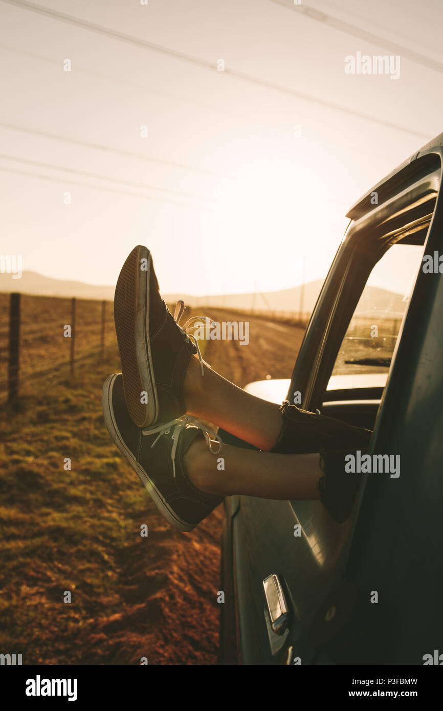 Close up of legs of a relaxing woman hanging out from car on a highway ...