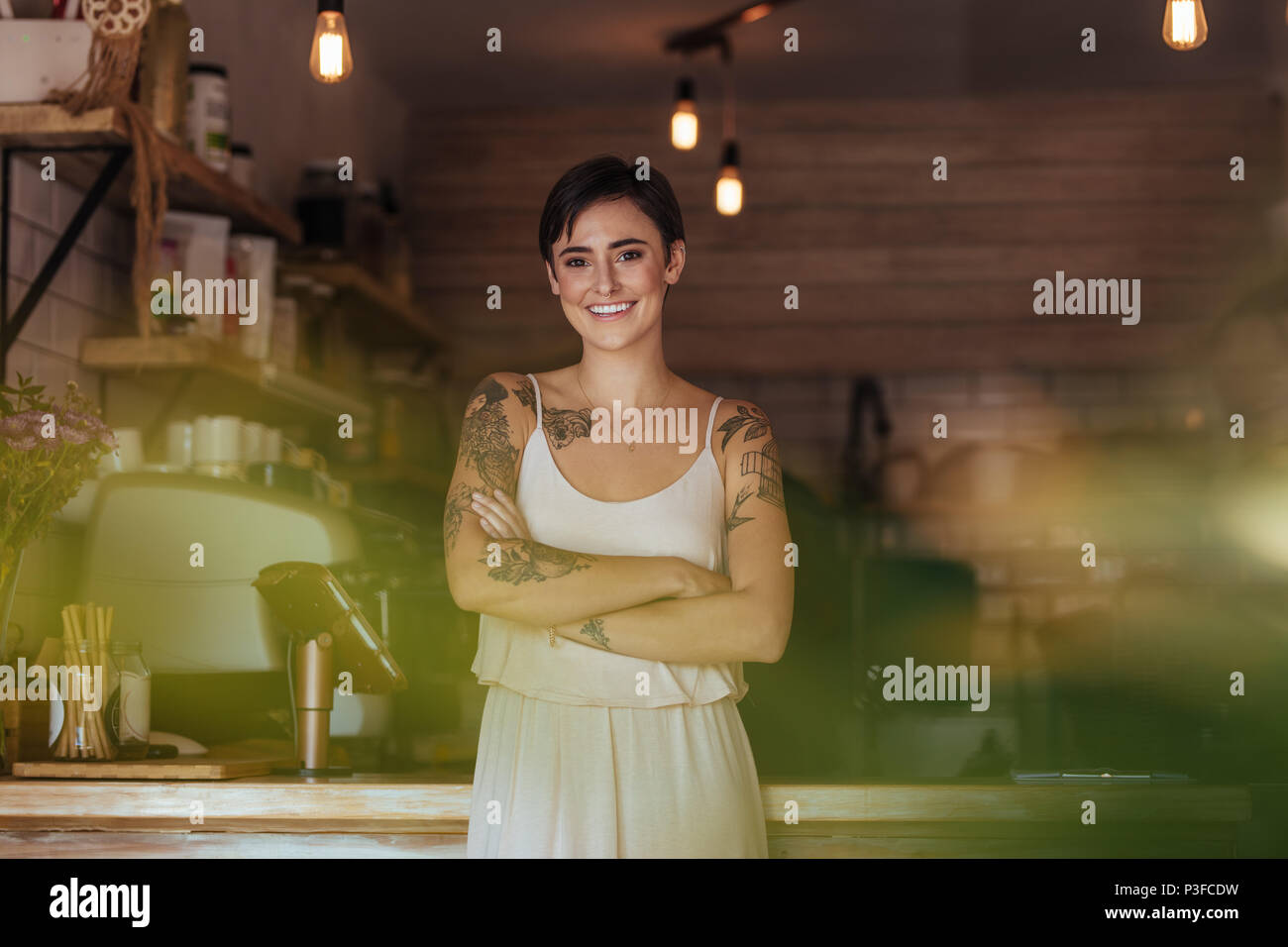 Woman standing in front of the counter of her cafe with folded arms ...