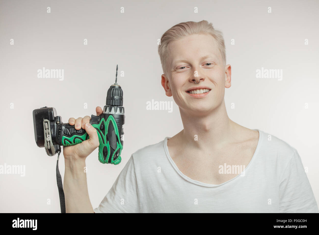 Portrait of a smiling handsome young man holding drill against white ...