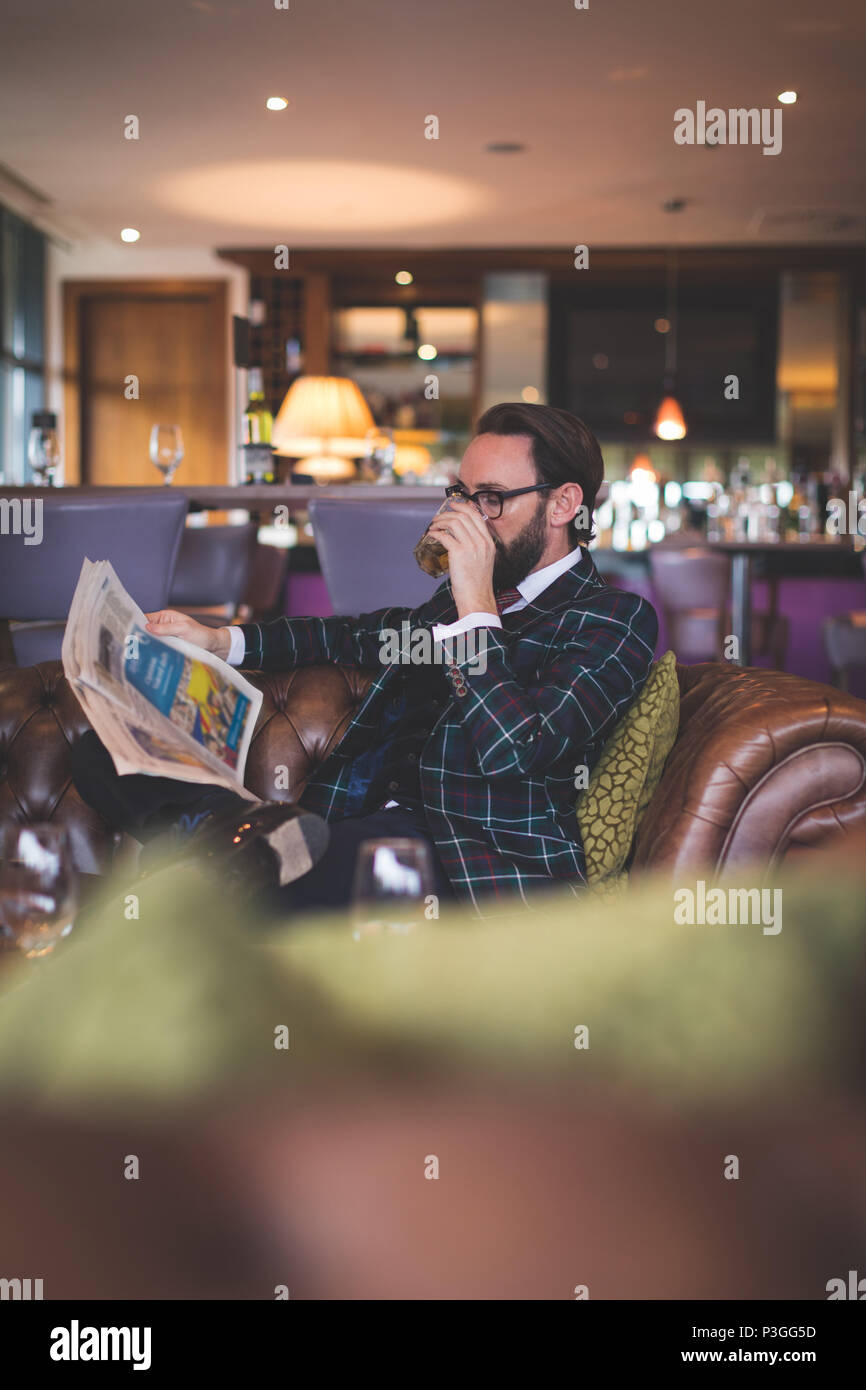 Businessman reading newspaper while having whisky Stock Photo - Alamy