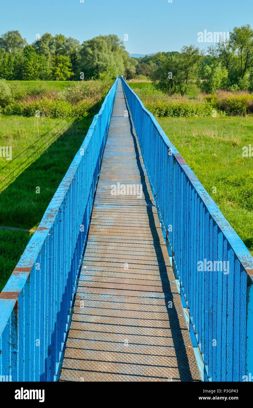 Springtime rural landscape. Metal footbridge over the river in the ...