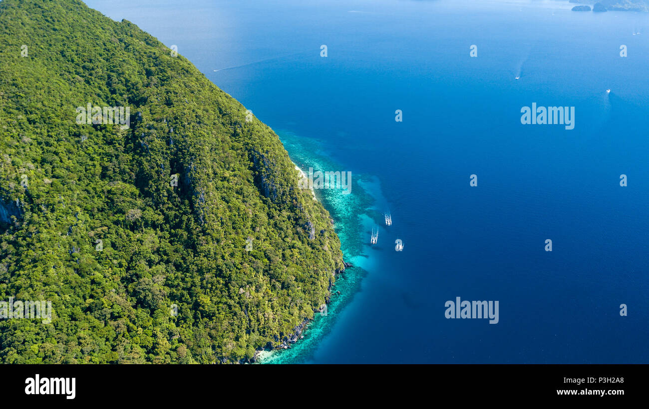 Aerial drone view of boats in a clear ocean, over a tropical coral reef ...