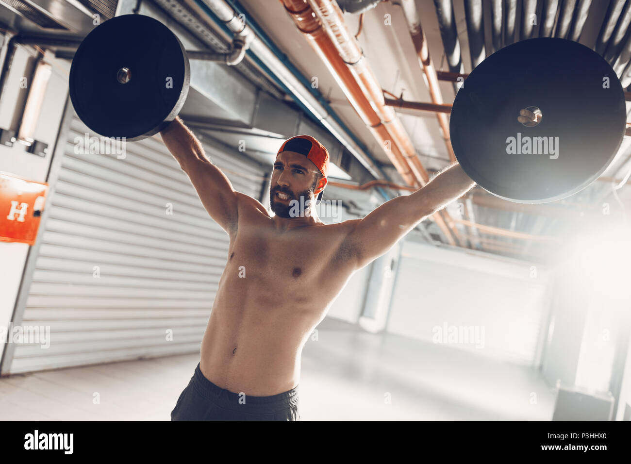 Young muscular man doing hard exercise with plate weights for shoulders ...