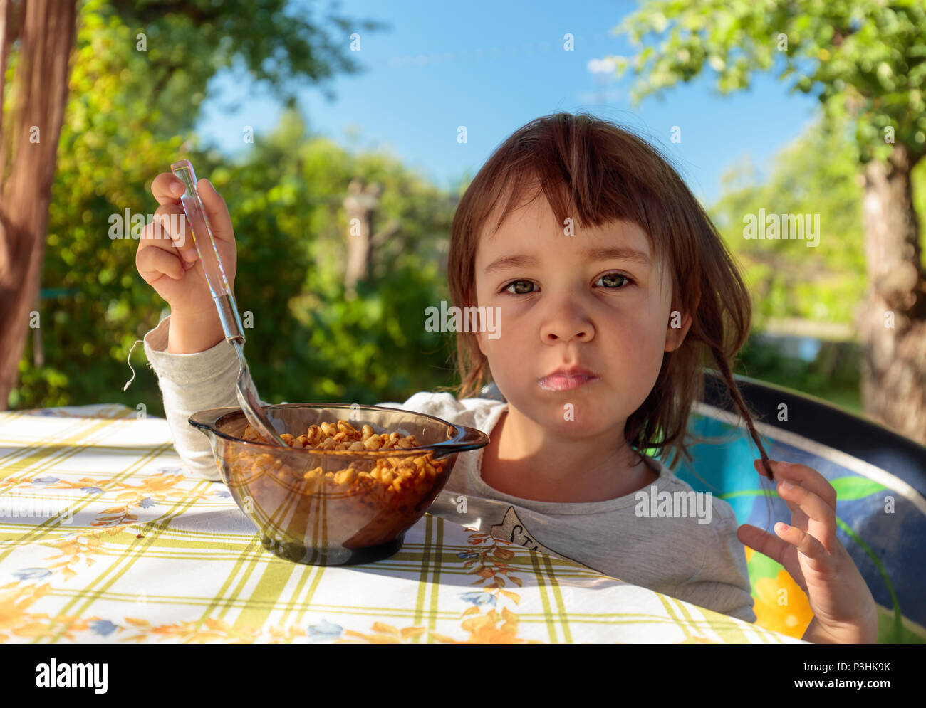 Cute little girl eat flakes with milk . Summer sunny day in the garden ...