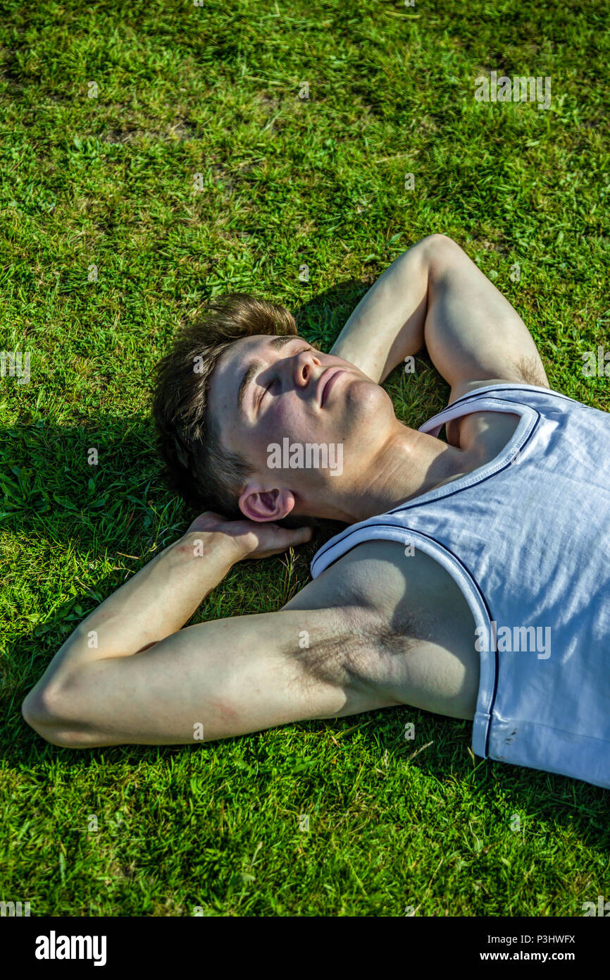 A young adult male sunbathing, laying on short grass on a warm summer's ...