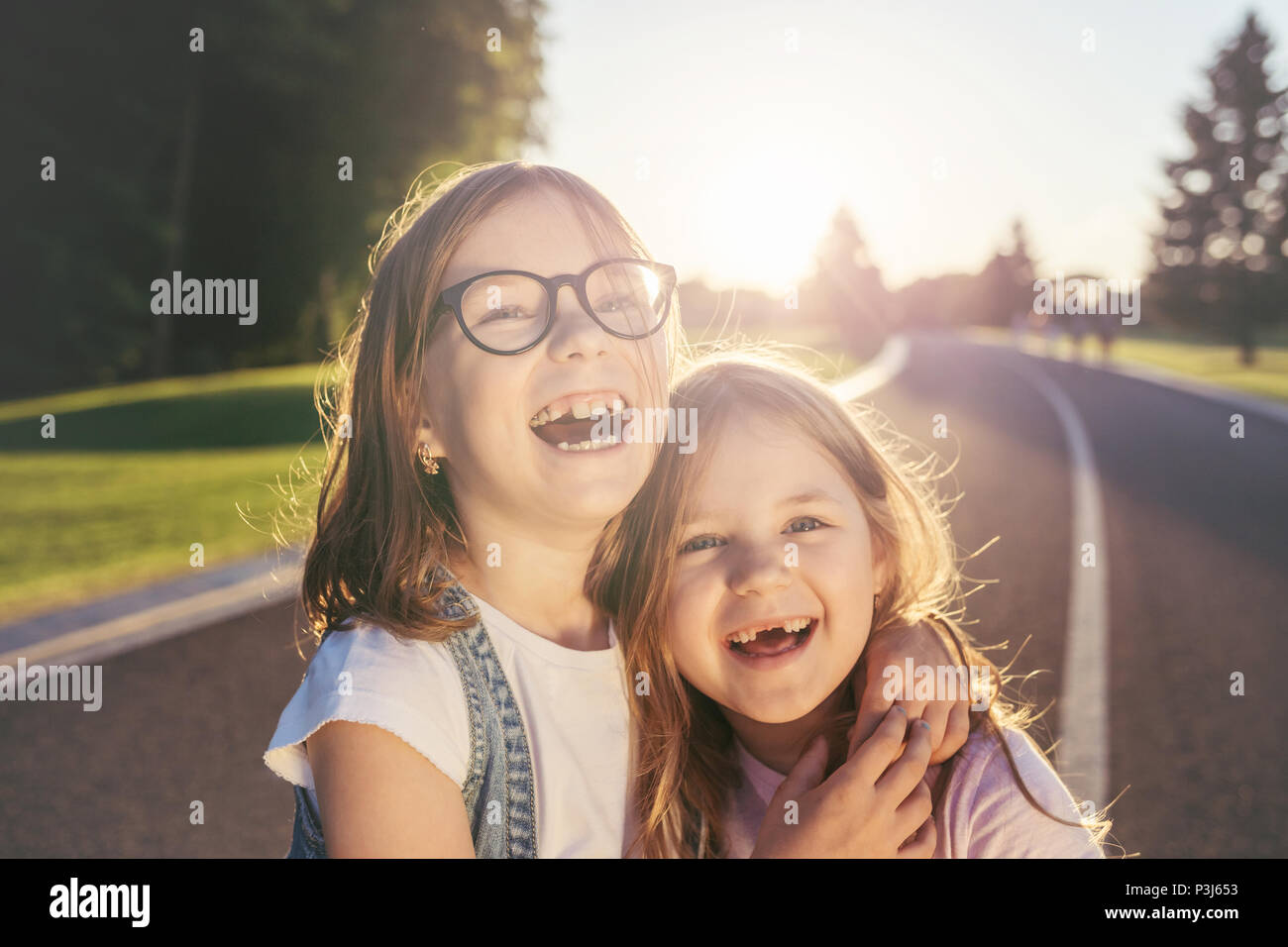 Two cheerful girls standing on the road, hugging and smiling against ...