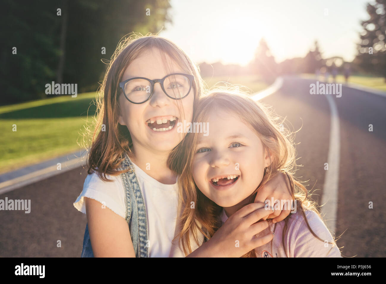 Two joyful girls standing on the road, hugging and smiling against the ...