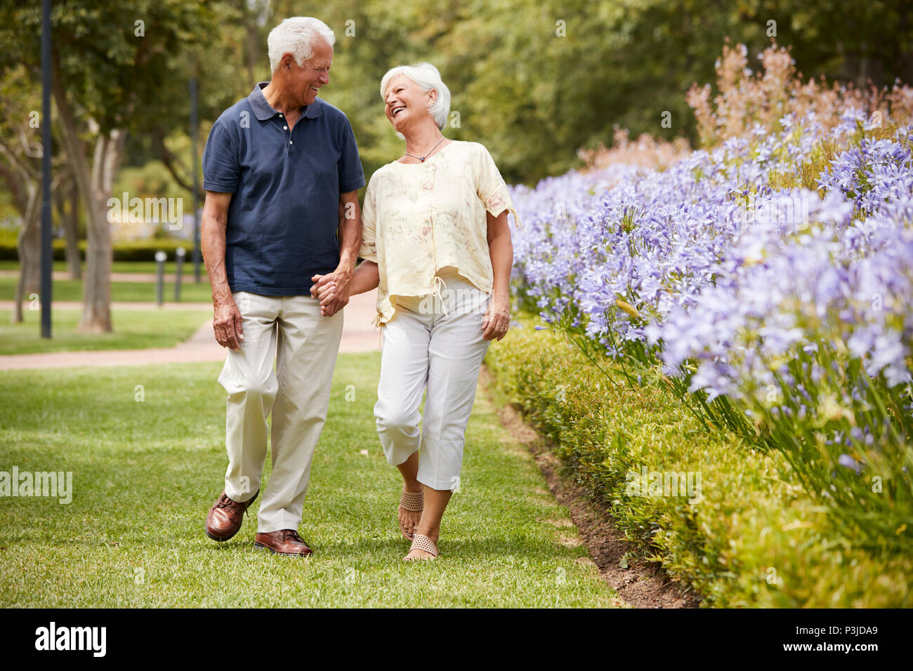 Senior Couple Holding Hands On Romantic Walk In Park Together Stock