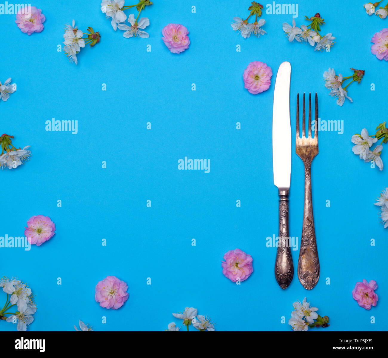 iron fork and knife on a blue background among the buds of flowers, top ...