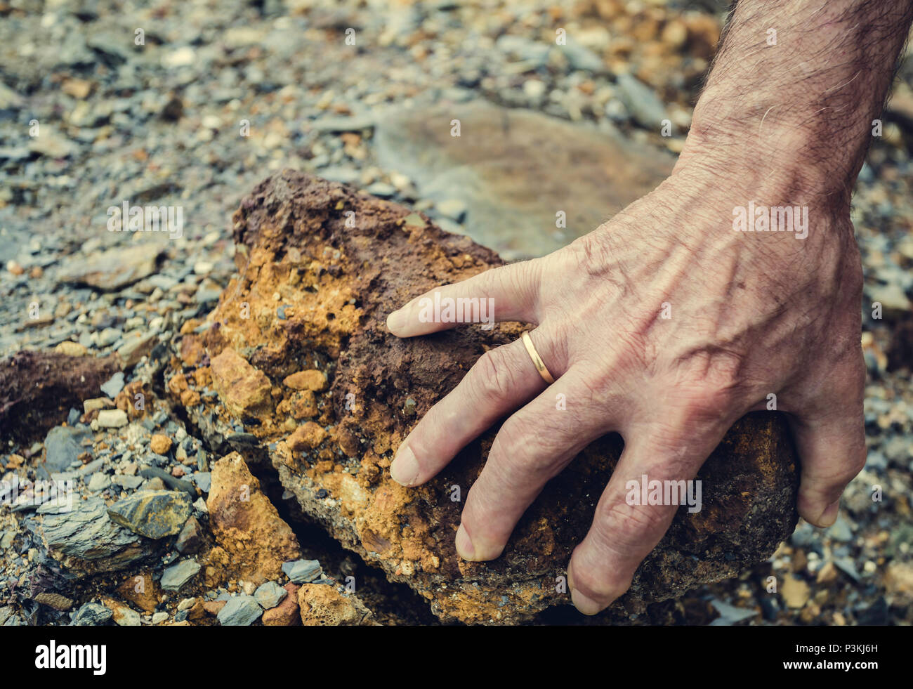 Senior person hand lifting a stone from the ground with the colors of ...