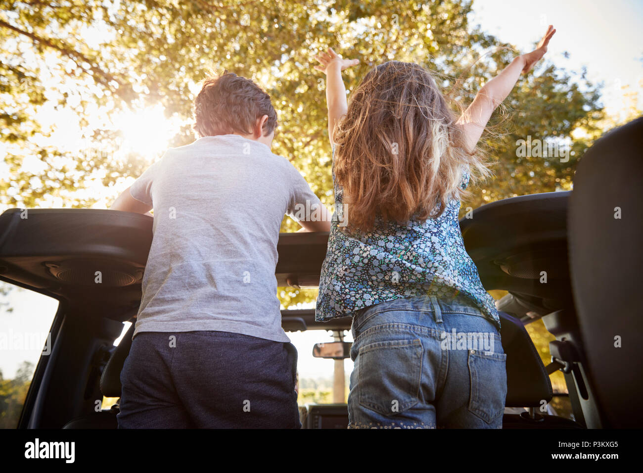 Children Standing Up In Back Of Open Top Car On Road Trip Stock Photo ...
