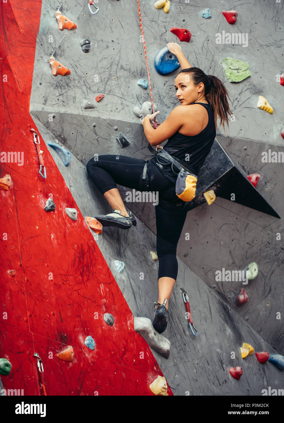 Fit sporty student girl moving up at rock climbing wall at the gym ...