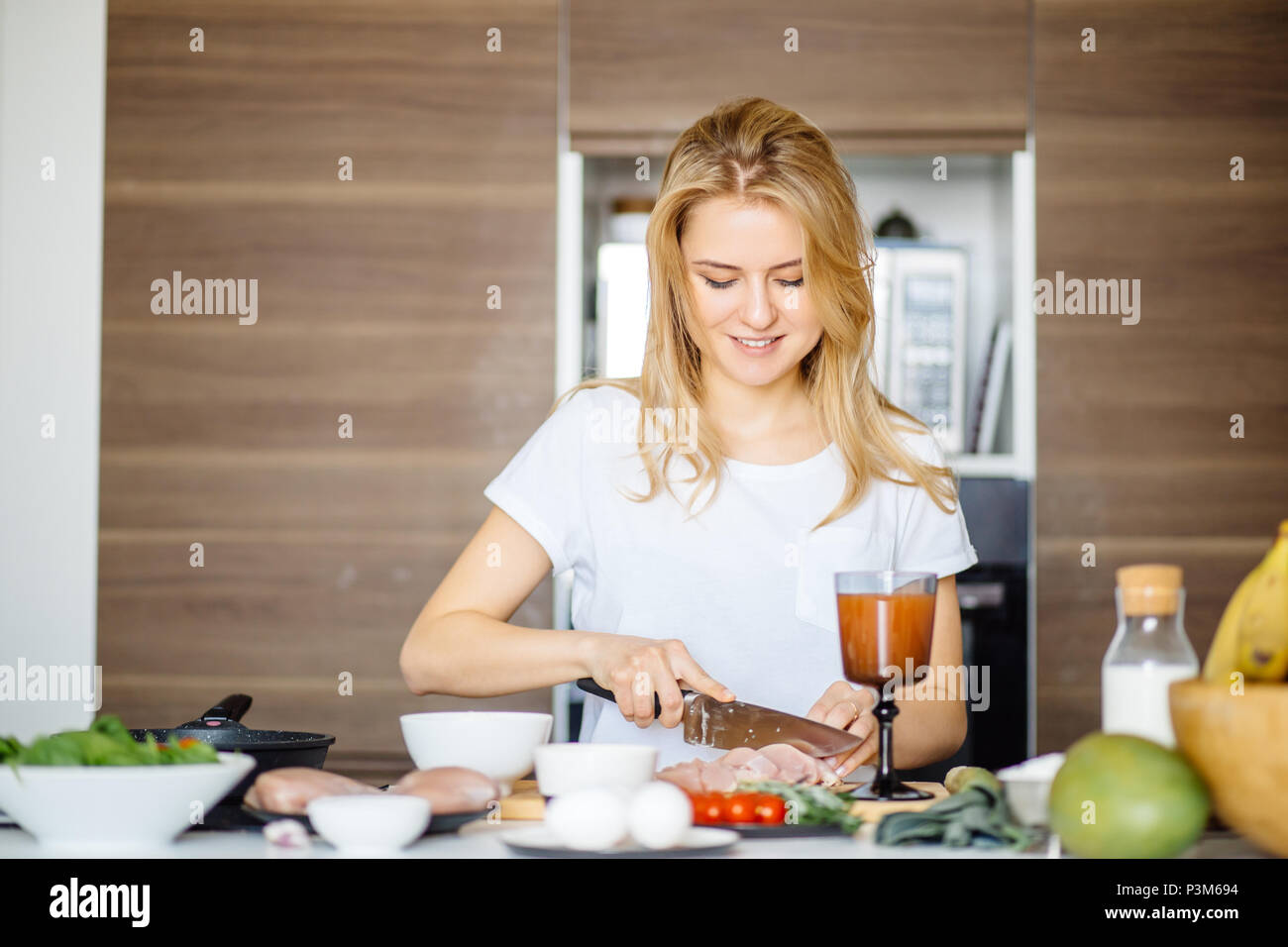 Woman cutting chiken meat on a kitchen table with a big Chef knife ...