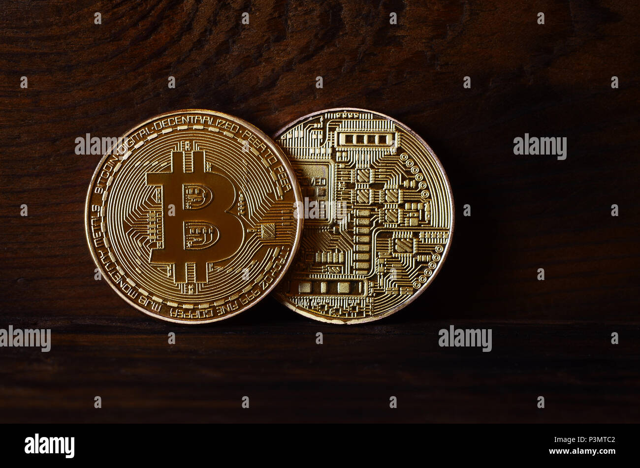 Two new golden physical bitcoins lies on dark wooden backgound, close ...