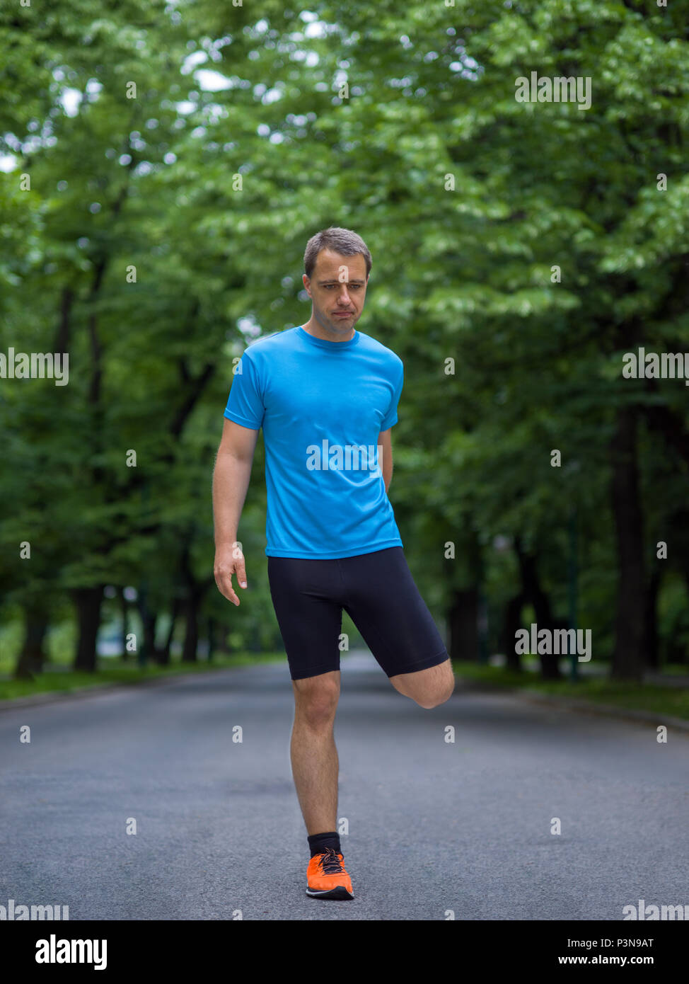 healthy male runner warming up and stretching in city park before ...