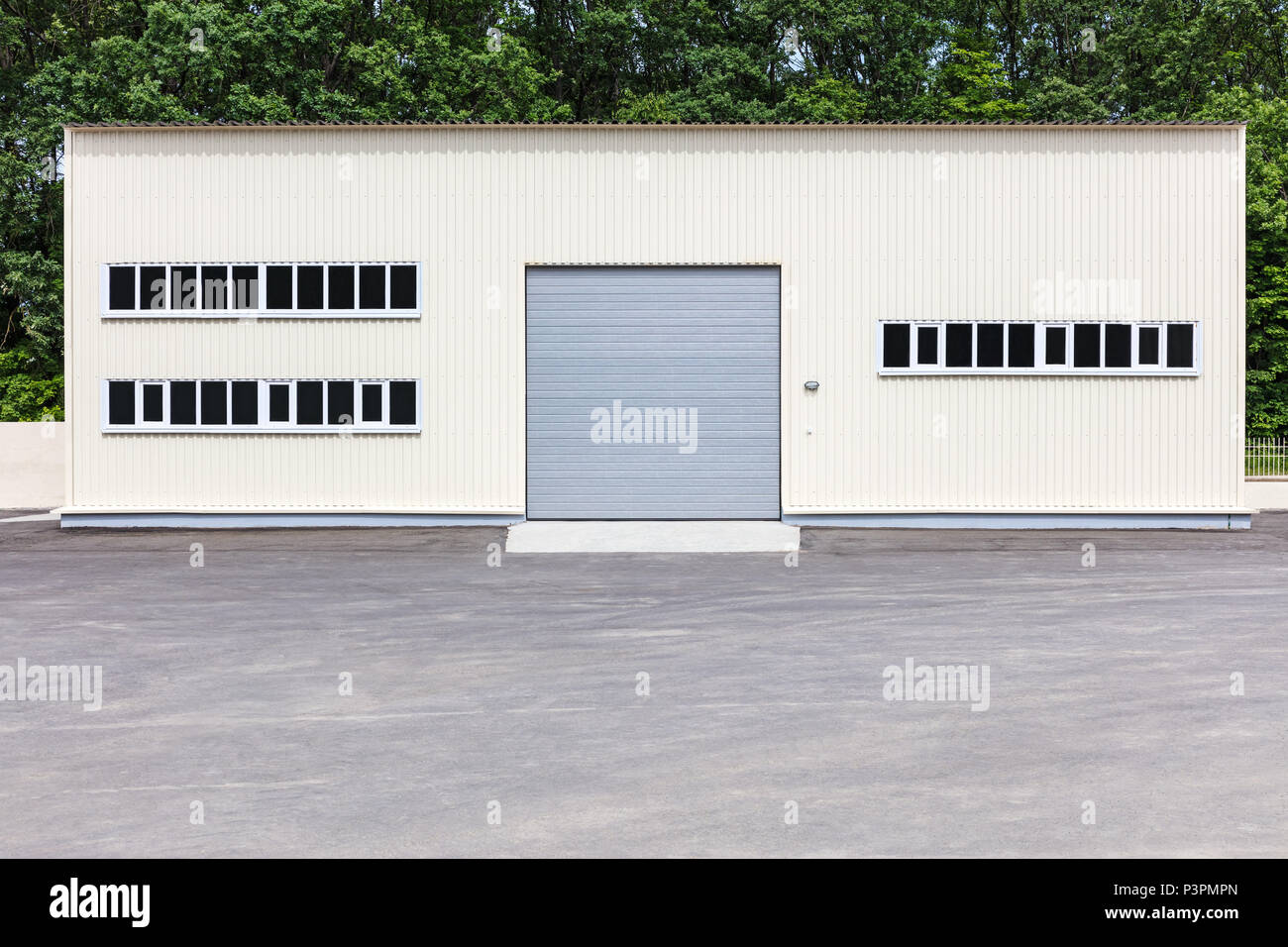 white industrial building facade with closed grey roller shutter gate ...
