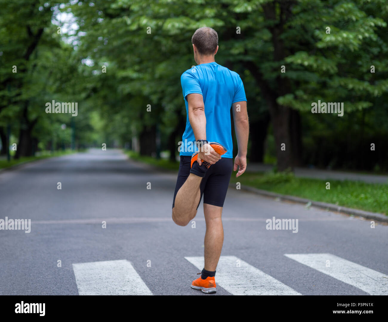 healthy male runner warming up and stretching in city park before ...