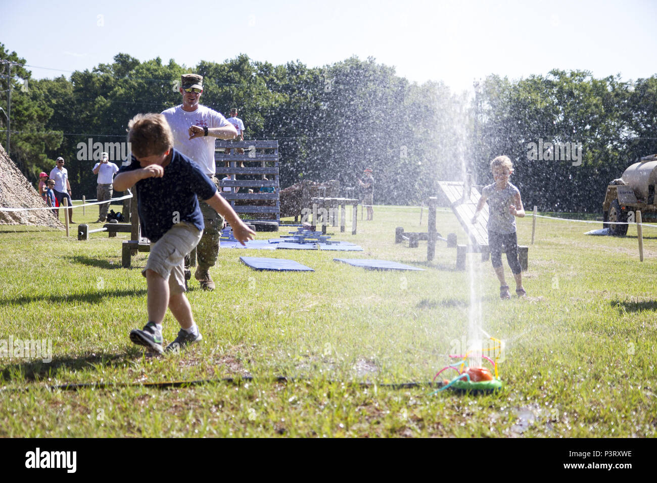 Children run through a sprinkler to the obstacle course’s finish line ...