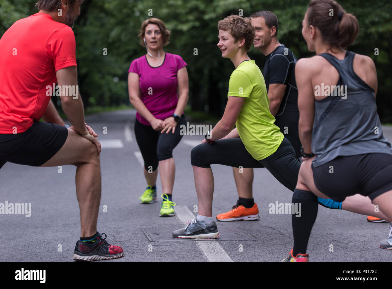 healthy runners team warming up and stretching in city park before ...