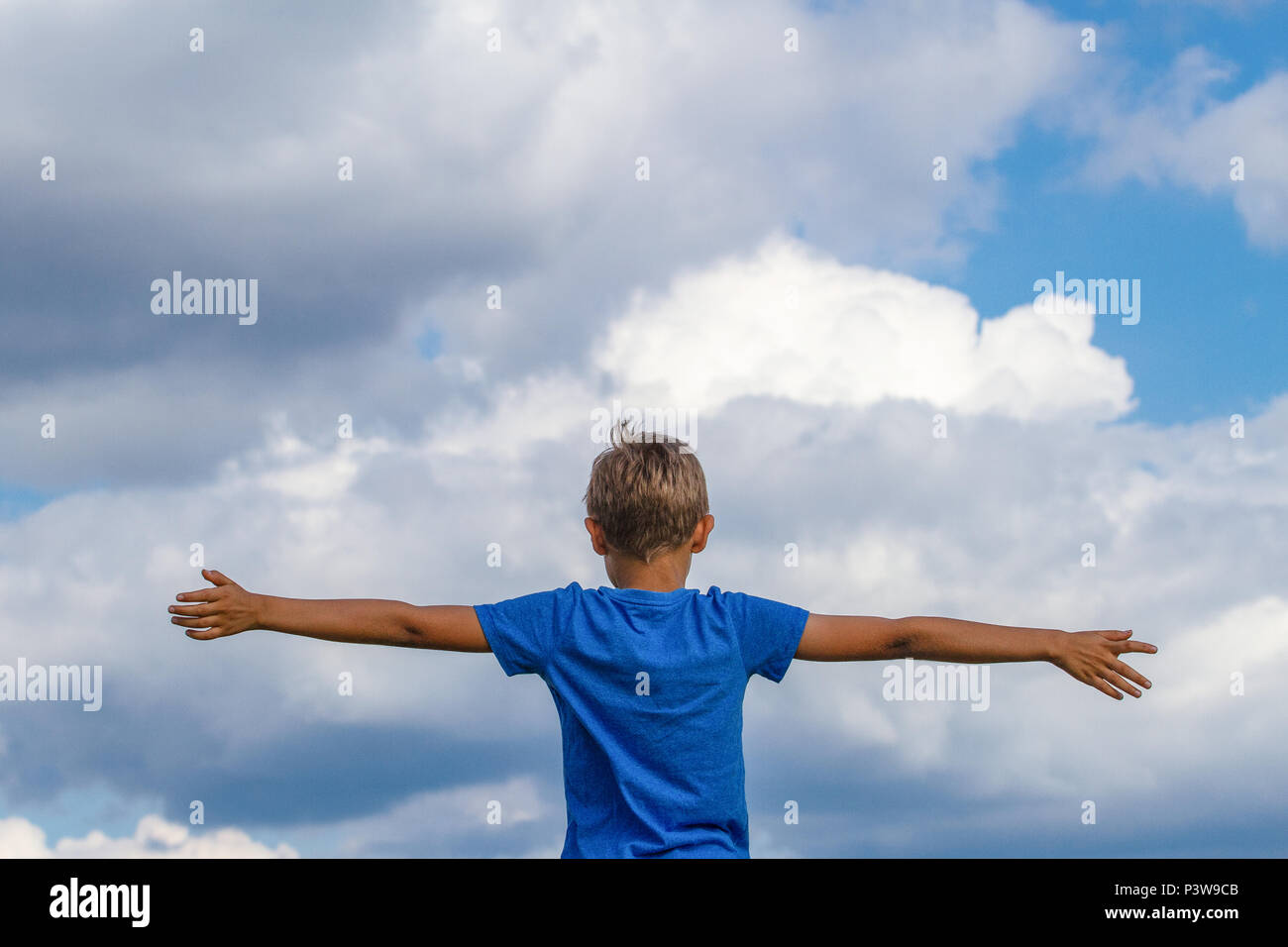 Happy kid with raised arms against blue sky. Freedom, joy and happiness ...