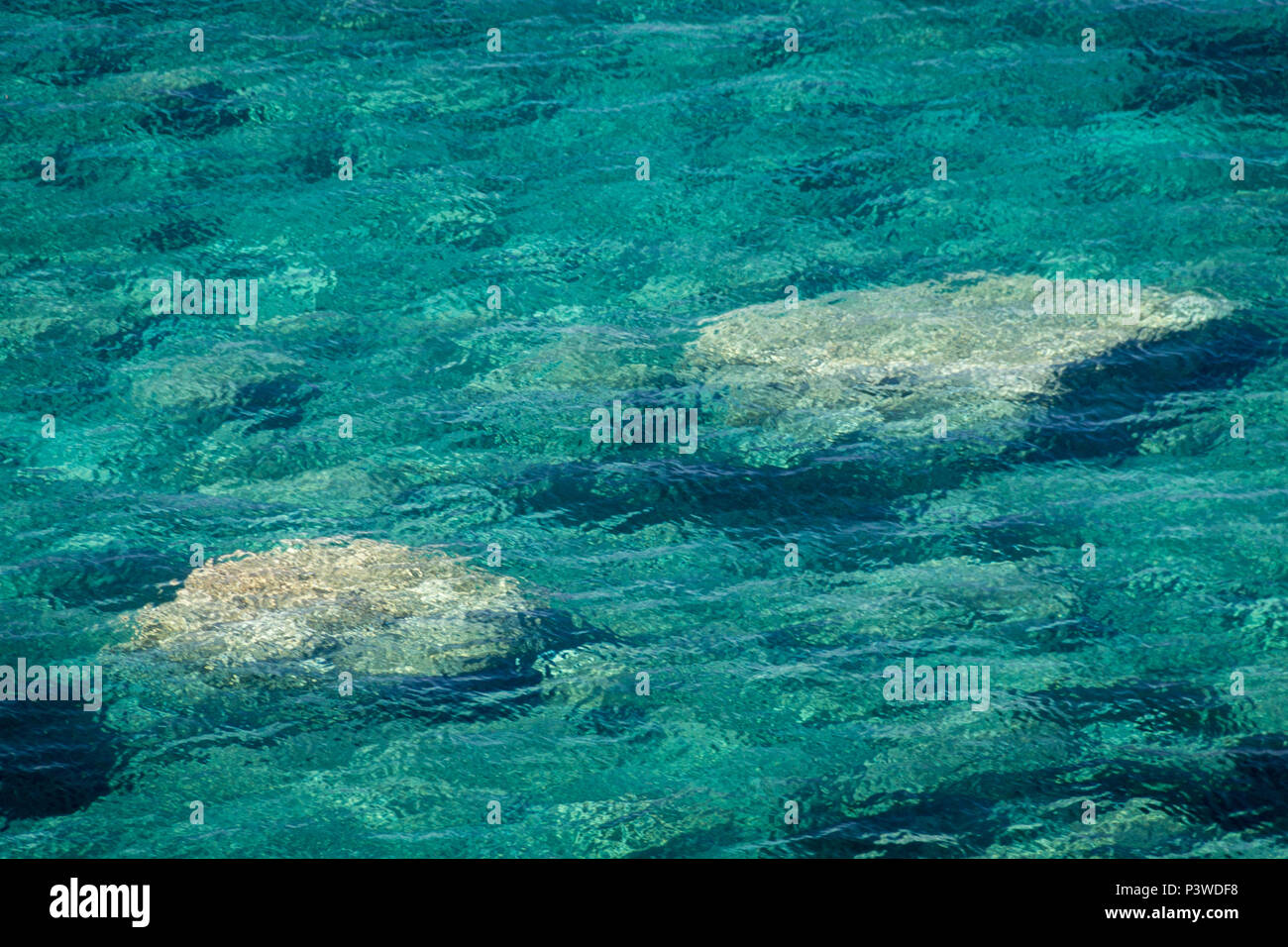 Texture of emerald colored ocean water with two stones shining through ...