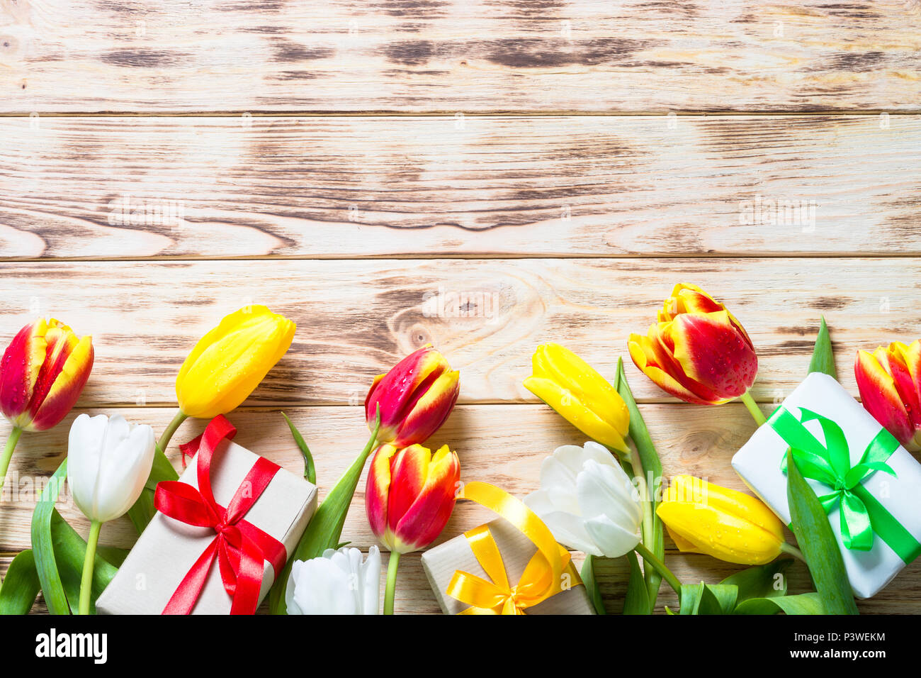 Holiday background. Tulips flower and present box on wooden table. Top ...