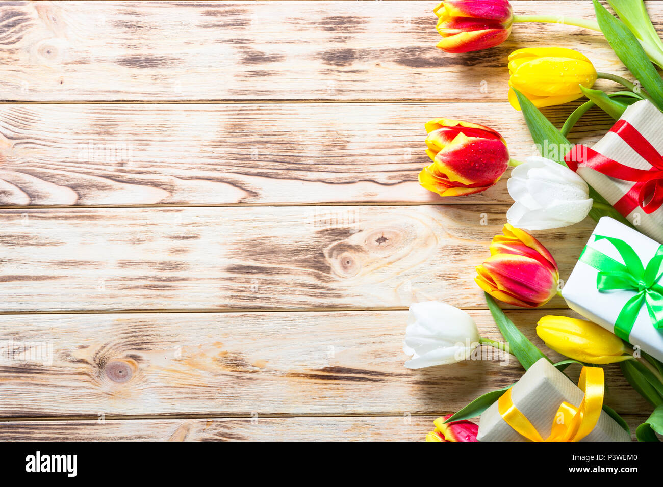 Holiday background. Tulips flower and present box on wooden table. Top ...