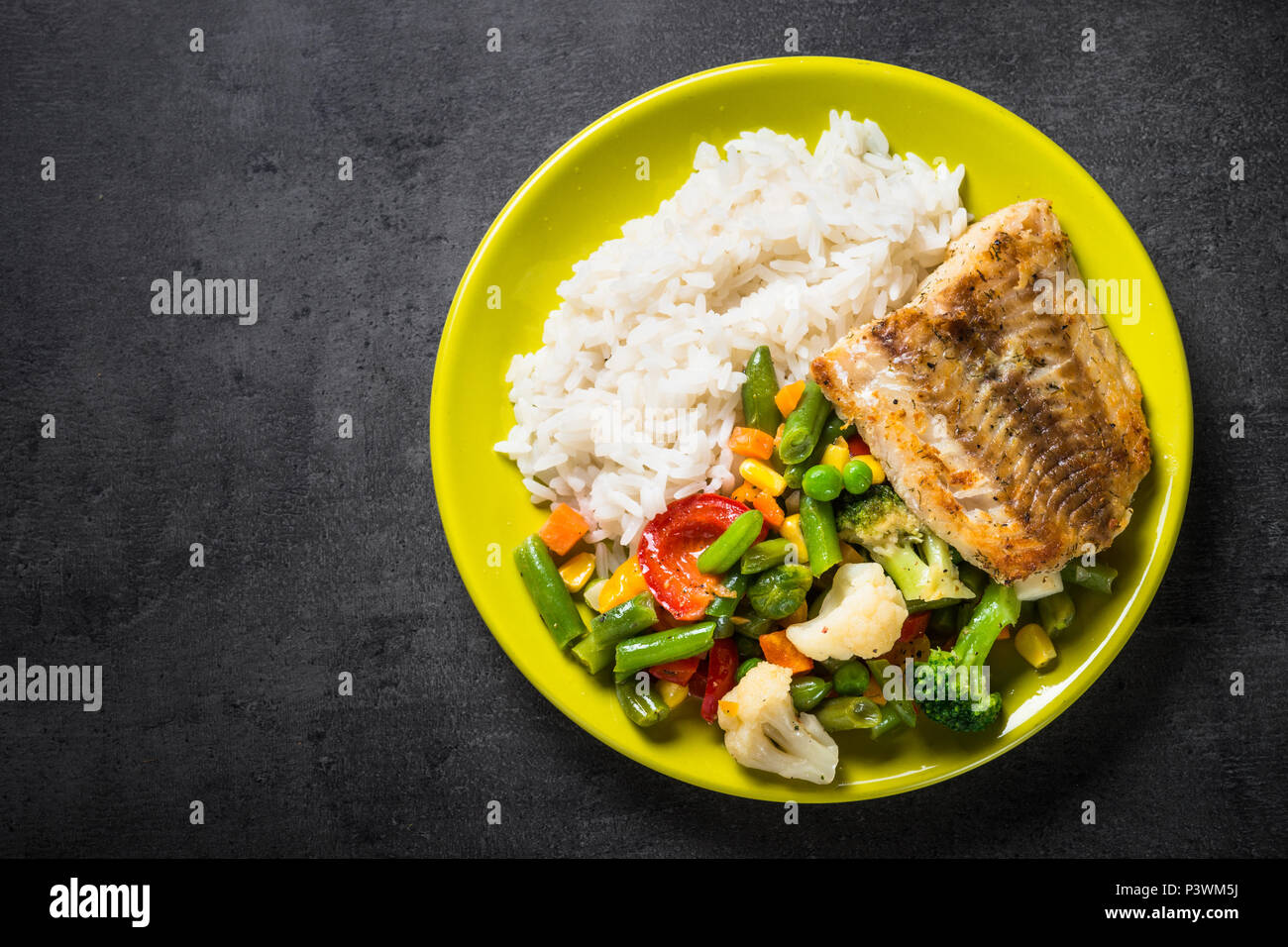 Fish, rise and vegetables in green plate on black background. Healthy ...
