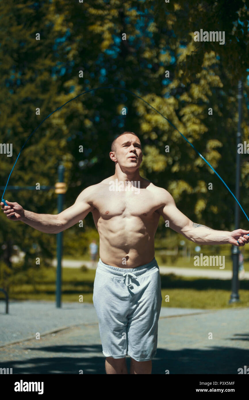 Athletic muscular man jumping with a rope, workout outdoors at sunny ...