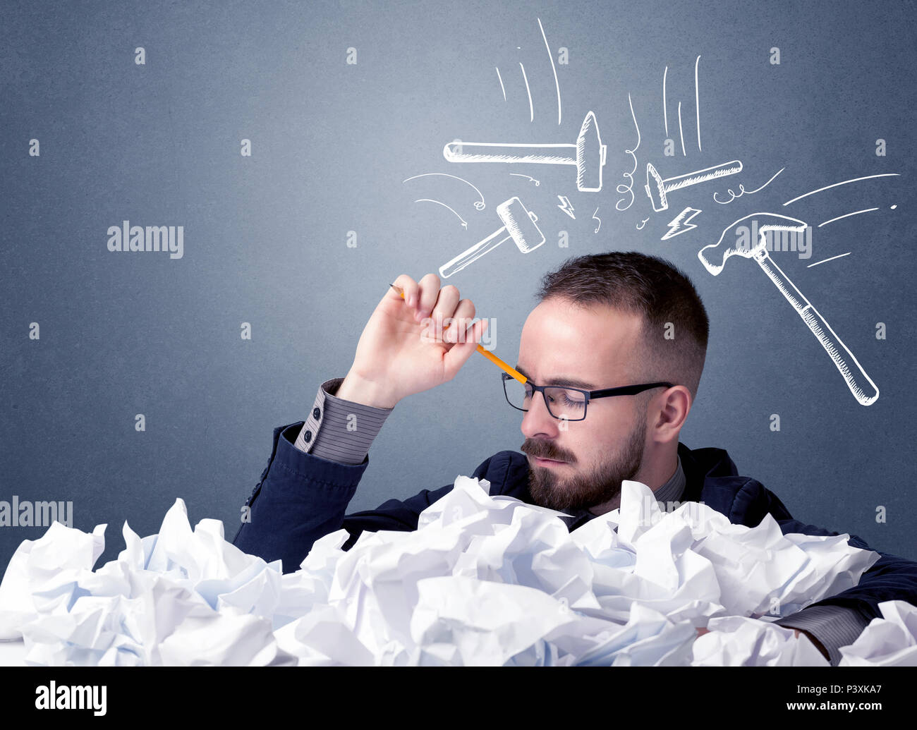 Young businessman sitting behind crumpled paper with drawn hammers ...