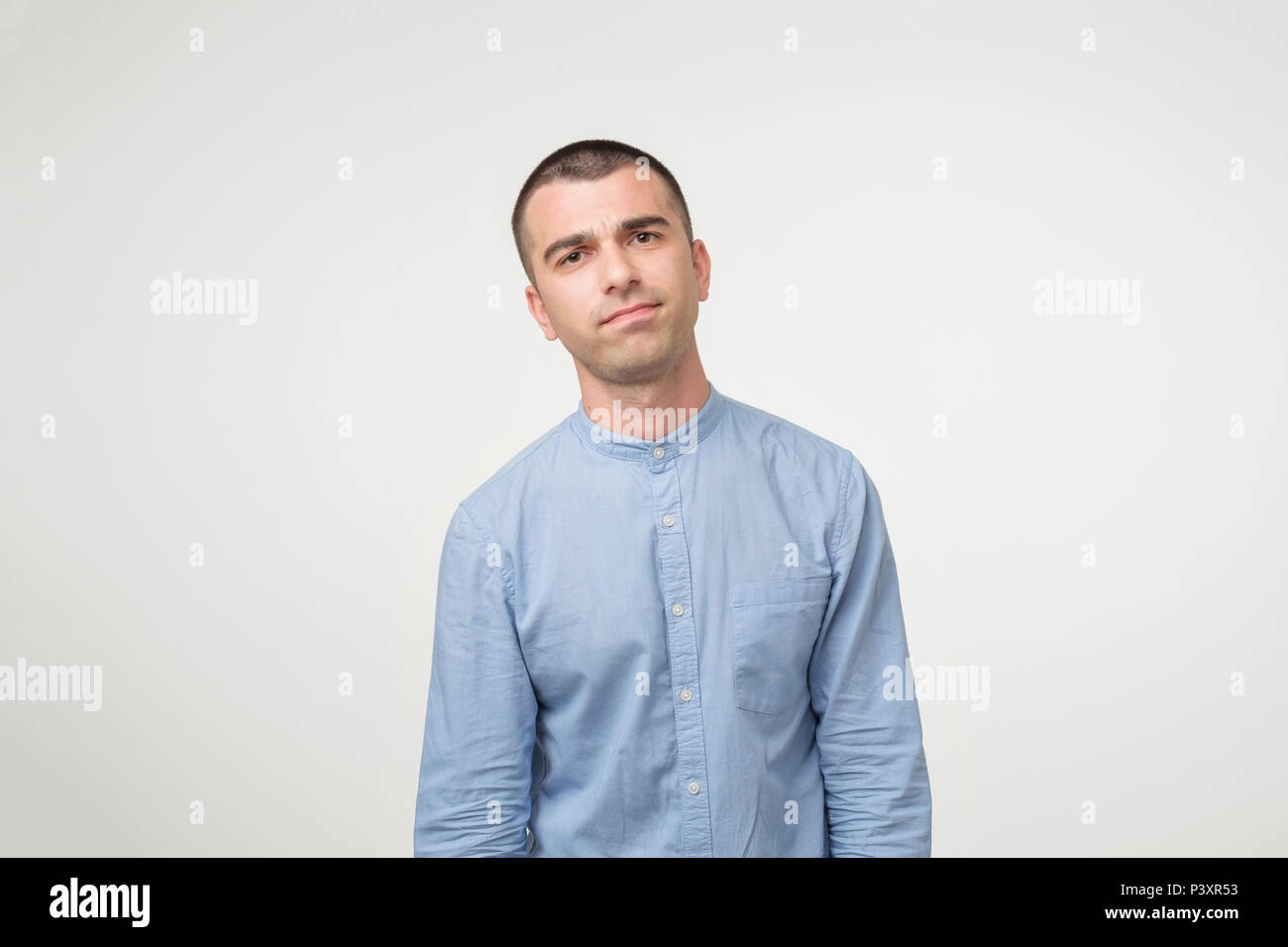 Close up of a doubtful young man in blue shirt. He is not sure what to ...