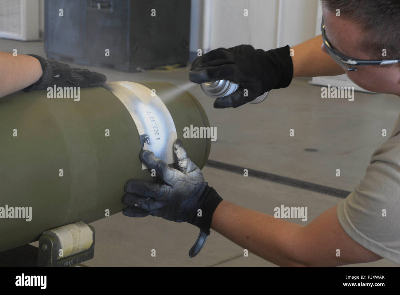An Airman from the 5th Munitions Squadron, spray paints the ...