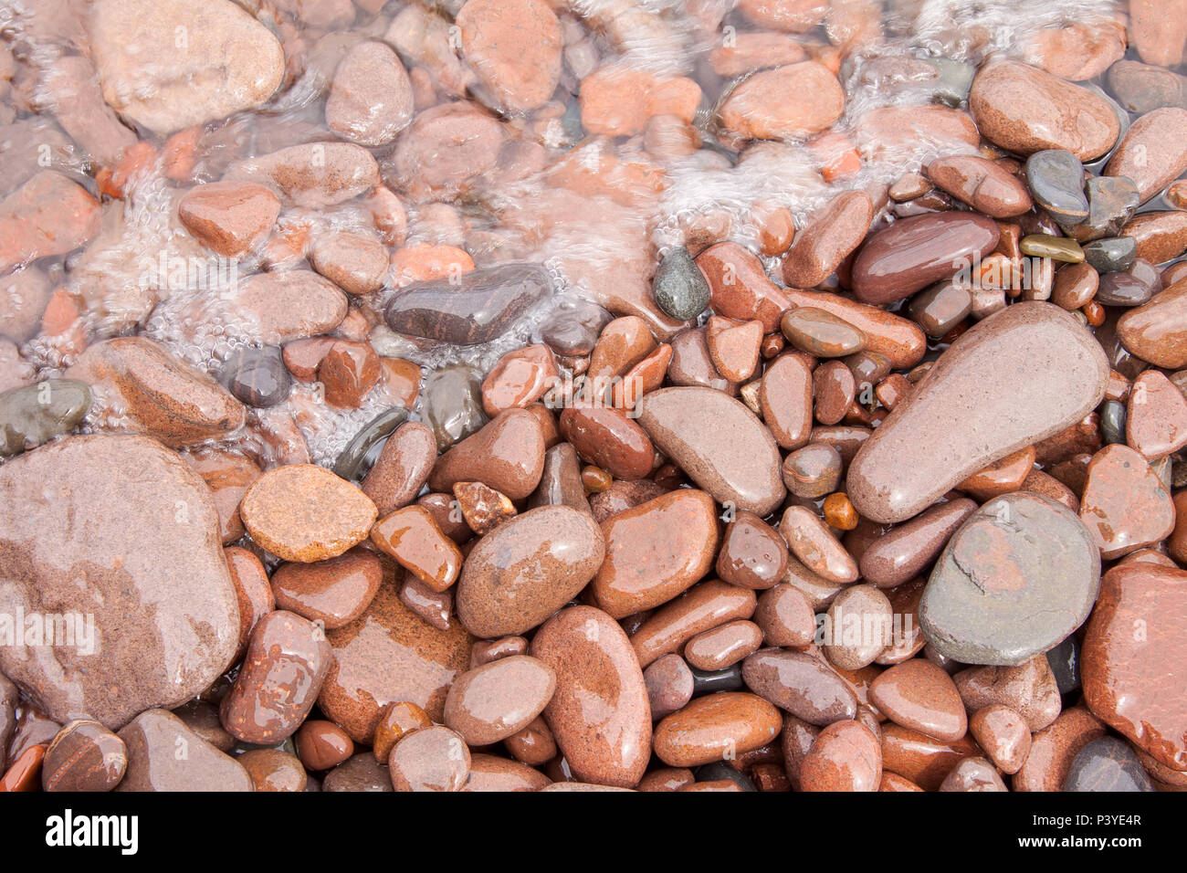 Waves wash over smooth rounded colorful rocks Stock Photo - Alamy