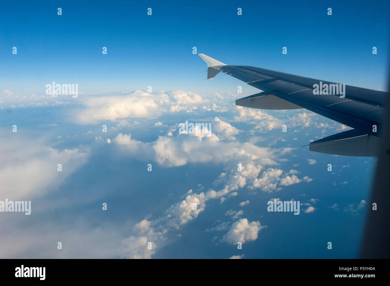 View from plane window of clouds and land below with wing in view Stock ...