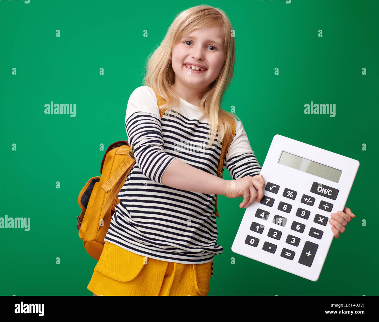 happy school girl with backpack showing calculator isolated on green ...