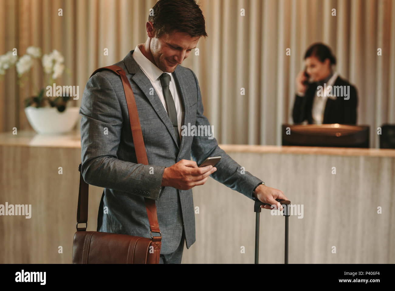 Happy businessman in hotel lobby using cellphone. Male guest arriving ...