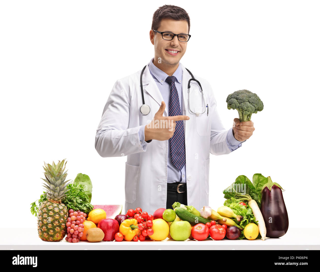 Doctor with broccoli pointing behind a table with fruit and vegetables ...