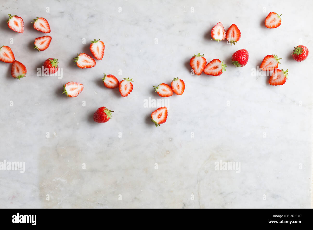 Mixture of whole and halved strawberries scattered on white marble ...